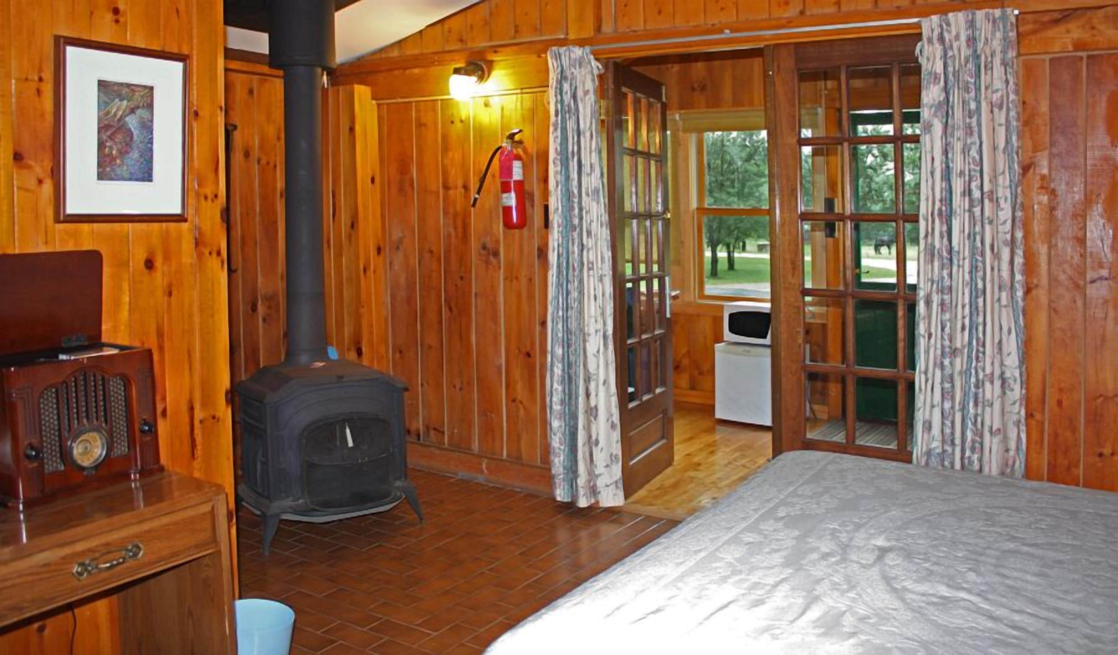 Um quarto de madeira com uma cama, um rádio antigo, uma lareira e uma porta que dá para o exterior.