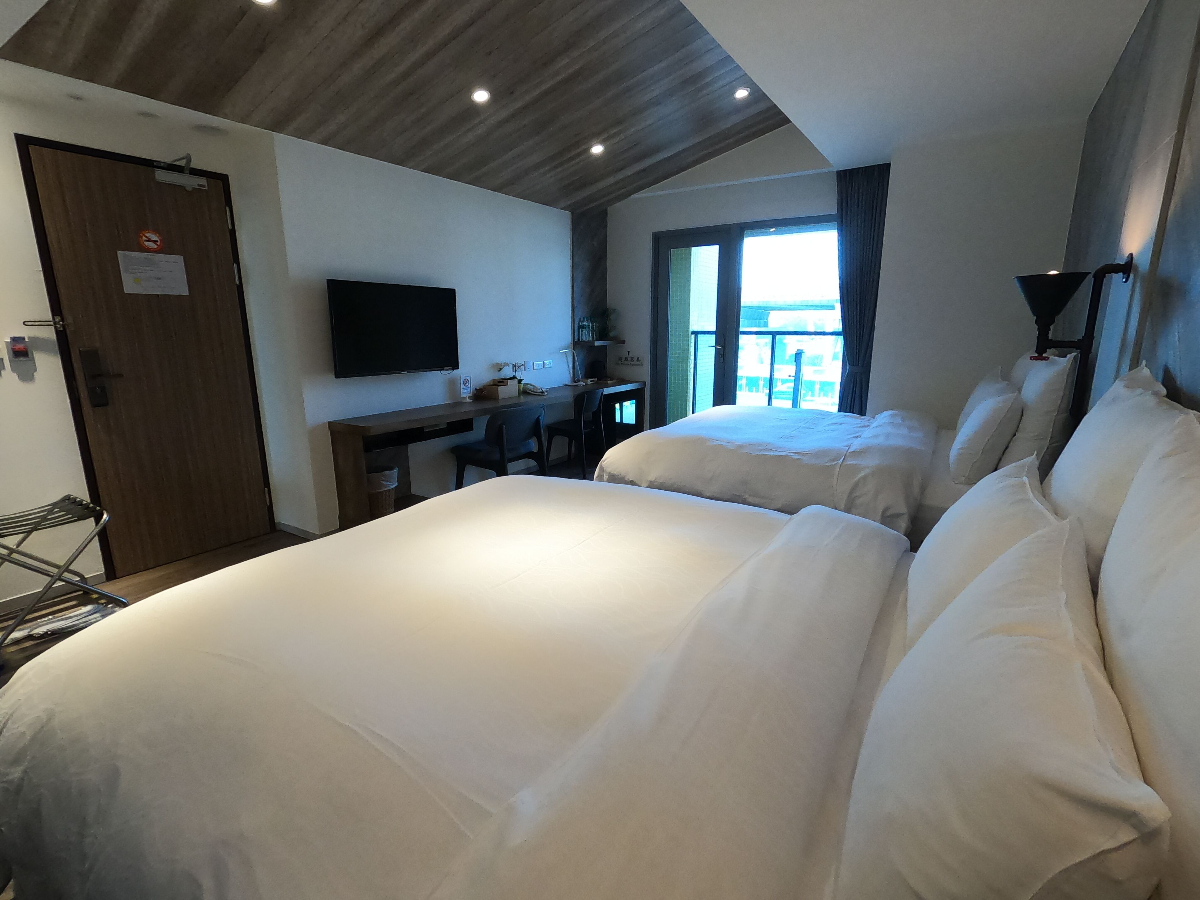 Quarto de hotel com duas camas, uma escrivaninha, televisão e janela com vista.
