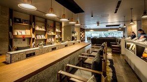 Uma área de bar moderna com mobiliário de madeira, ilumina ção pendente e um balcão com diversos objetos.