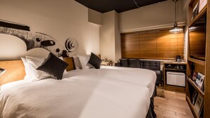 Quarto de hotel moderno com uma cama grande, uma secretária pequena, uma kitchenette e uma estante de livros.