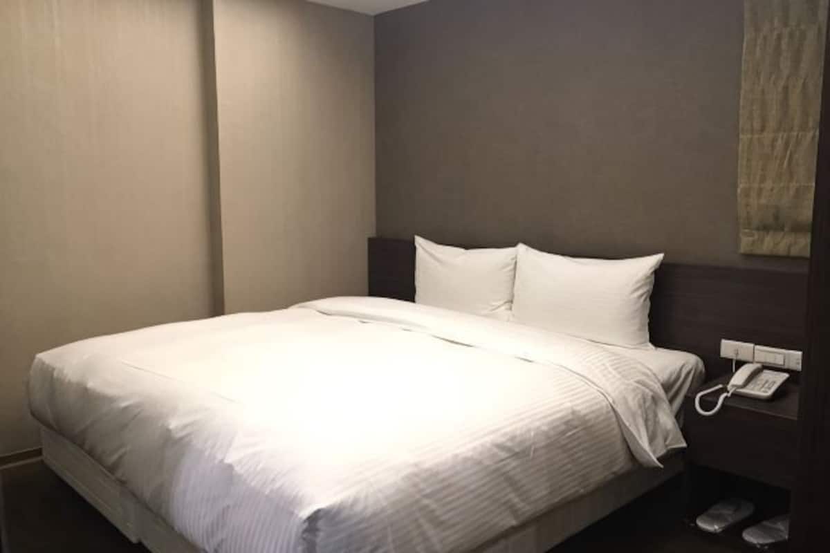 Quarto de hotel com cama, telefone ao lado e sapateira.