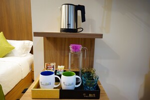 Quarto de hotel com cama, mesinha com cafeteira, chávenas e um copo.