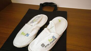Um par de chinelos brancos com a inscrição "five/6" e "HOTEL SPLENDOUR" estampada, colocados sobre um tapete preto.