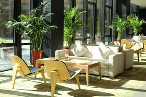 Um hall moderno com um sofá branco, duas poltronas amarelas, uma mesa de madeira e várias plantas em vasos.