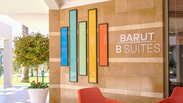 Entrada de um hotel com uma placa indicando "BARUT SUITES" e painéis verticais coloridos.