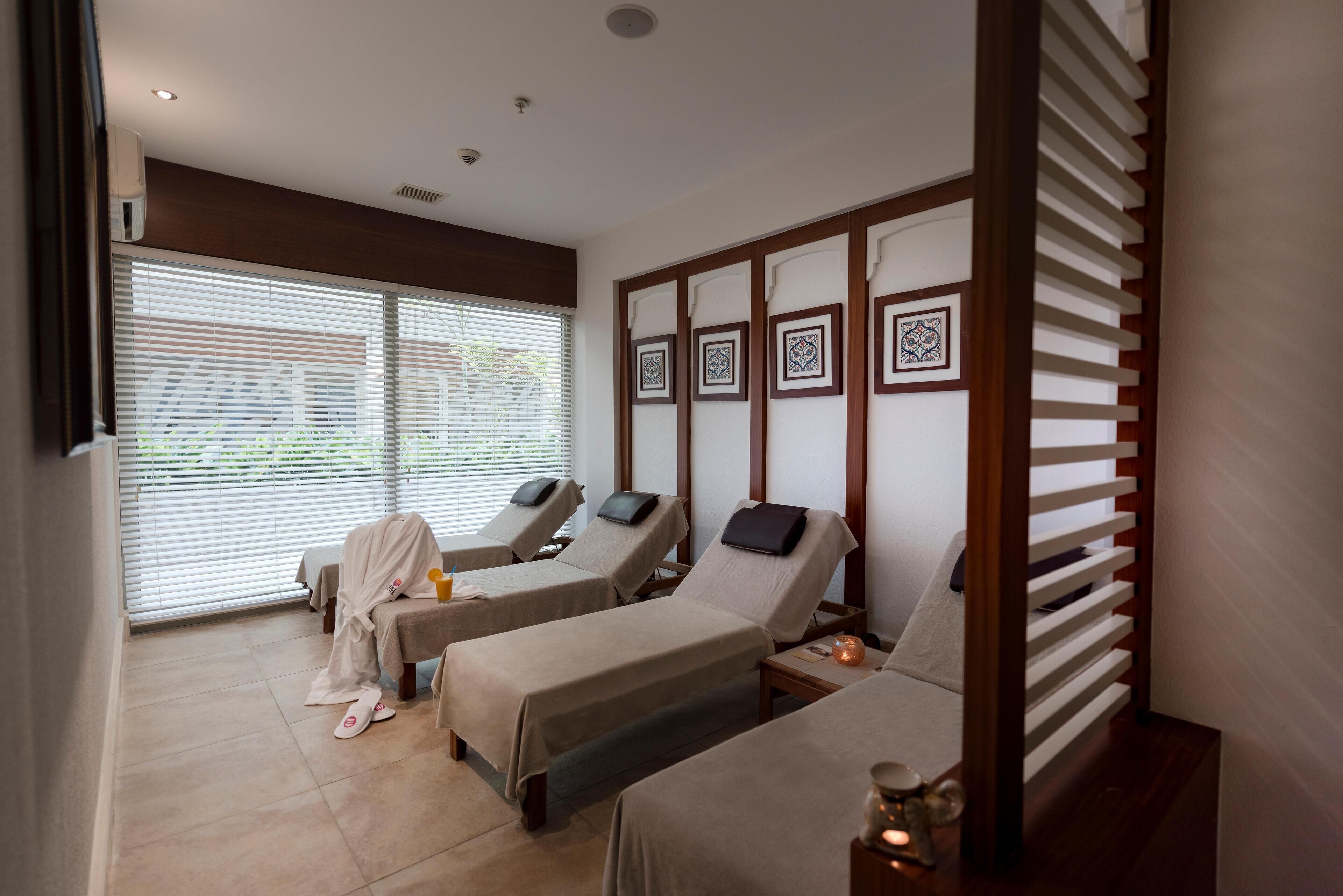 Uma sala de spa com três macas de massagem, ar condicionado no teto e uma grande janela com persianas.