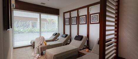 Uma sala de spa com três macas de massagem, ar condicionado no teto e uma grande janela com persianas.