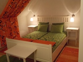Uma cama de solteiro com colcha verde e branca estampada, duas almofadas verdes e duas mesas de cabeceira com abajures.