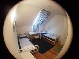 Um pequeno alojamento com uma cama de solteiro, uma secretária e uma cadeira.