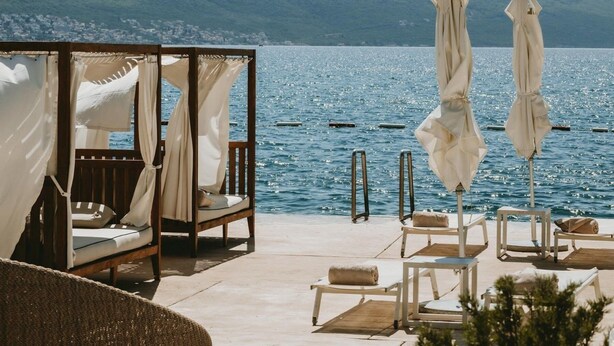 Um terraço à beira-mar com cama de dossel, cadeiras de descanso e guarda-sóis.