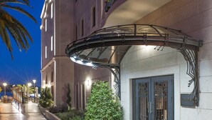Entrada de hotel com toldo curvo, portão e caminho bem iluminado.