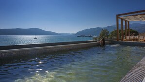 Piscina translúcida com vista para o mar e montanhas.