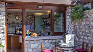 Um edifício rústico de pedra com área de bar, apresentando um barril de madeira, uma mesa de vidro e cadeiras de madeira com almofadas cor-de-rosa.