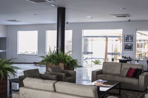 Um hall espaçoso com grandes janelas, uma coluna central preta e uma área de estar com sofás e uma mesa de centro.