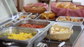 Buffet com diversos alimentos, incluindo cachorros-quentes, ovos mexidos e pão.