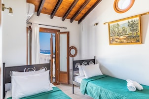 Quarto com duas camas, vista por uma porta aberta, um quadro na parede e teto de madeira.