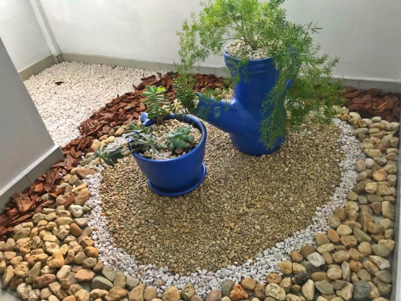 Um pequeno jardim cercado, com plantas em vasos e um caminho de cascalho.