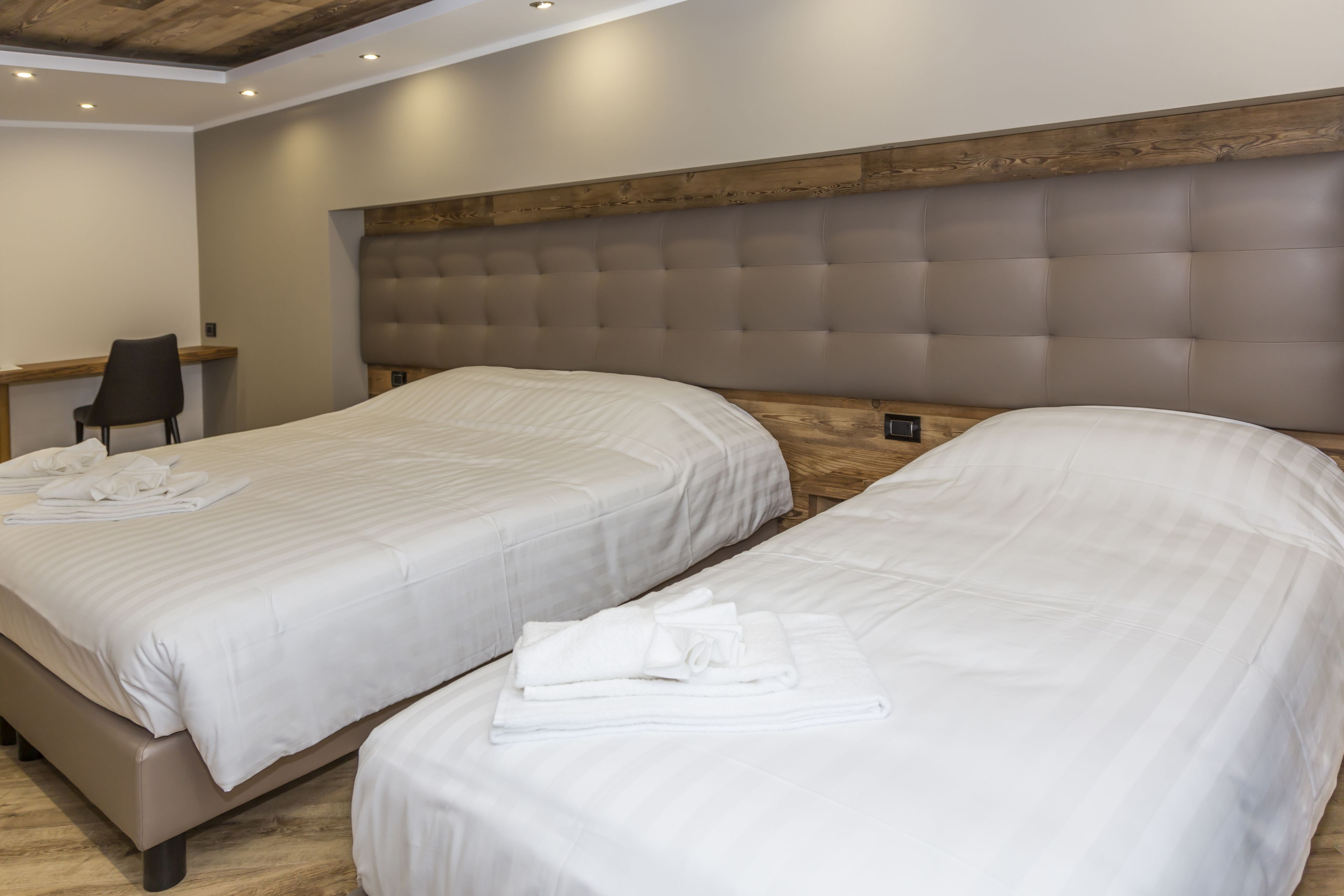 Quarto de hotel com duas camas, cabeceira de madeira, uma escrivaninha e uma cadeira.