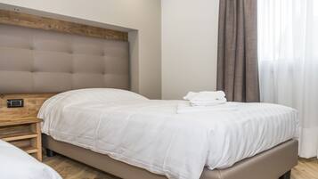 Quarto de hotel moderno com uma cama grande, cabeceira de madeira, mesa de cabeceira com abajur e uma janela com cortinas.