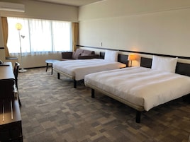 Quarto de hotel com duas camas, uma escrivaninha, uma cadeira, um abajur e uma janela com cortinas.