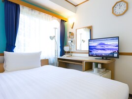 Quarto de hotel com cama, escrivaninha, computador, relógio e janela com cortinas.