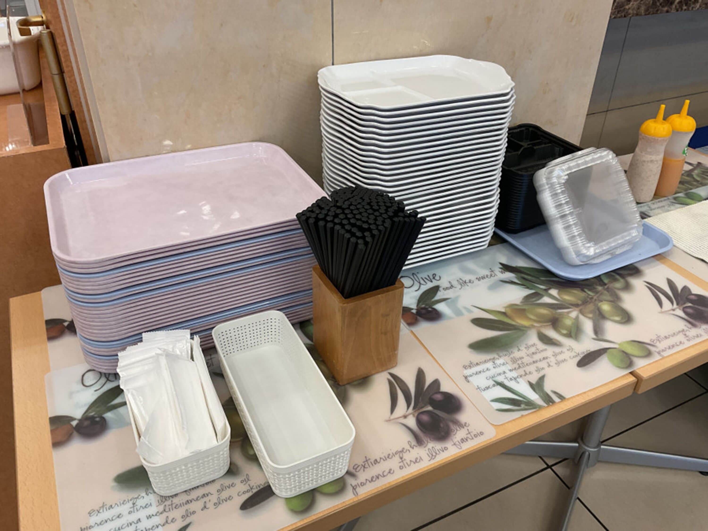 Uma mesa com pilhas de pratos brancos e pretos, um suporte de utensílios de madeira e uma bandeja com garrafas de azeite.