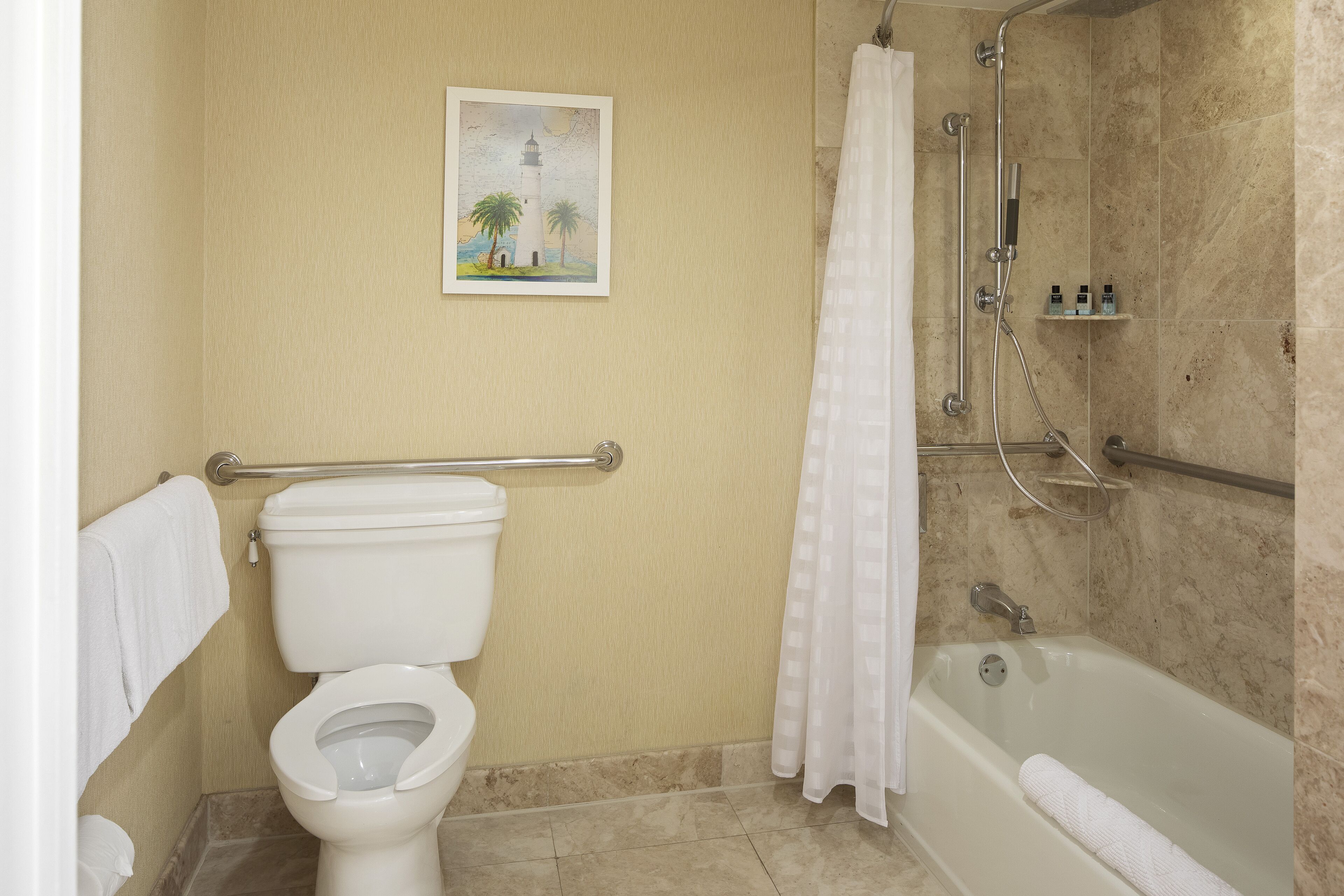 Casa de banho com sanita, chuveiro com porta de vidro, barra de apoio e um pequeno prateleira com artigos de higiene pessoal.