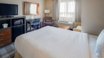 Quarto de hotel com uma cama grande, uma escrivaninha com computador, uma televisão, um micro-ondas e um ar condicionado.