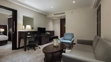 Quarto de hotel com cama, escrivaninha com cadeira, sofá, mesa de centro e televisão.