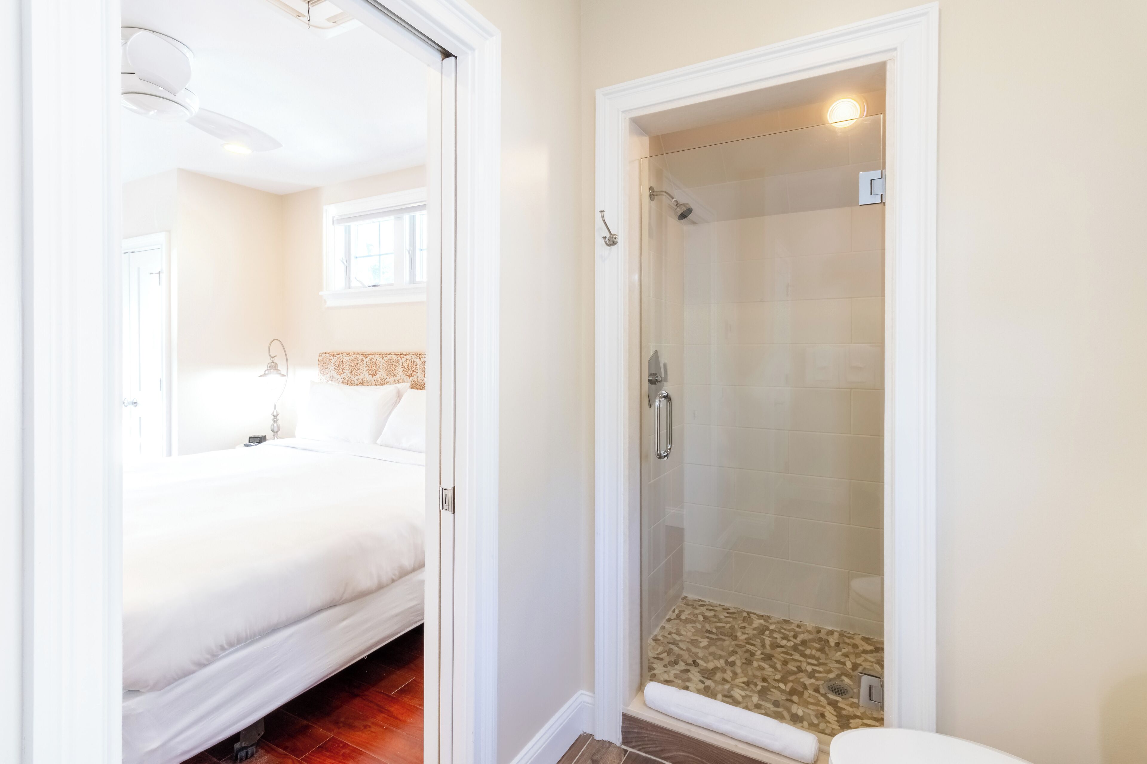 Quarto com cama, mesa de cabeceira e janela. Um banheiro adjacente ao quarto inclui chuveiro, vaso sanitário e pia.