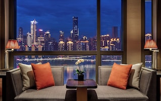 Sala de estar moderna com sofá, duas luminárias e vista para o horizonte urbano à noite.
