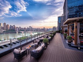 Terraço no telhado com área de estar externa, vista para um rio e horizonte urbano ao fundo.