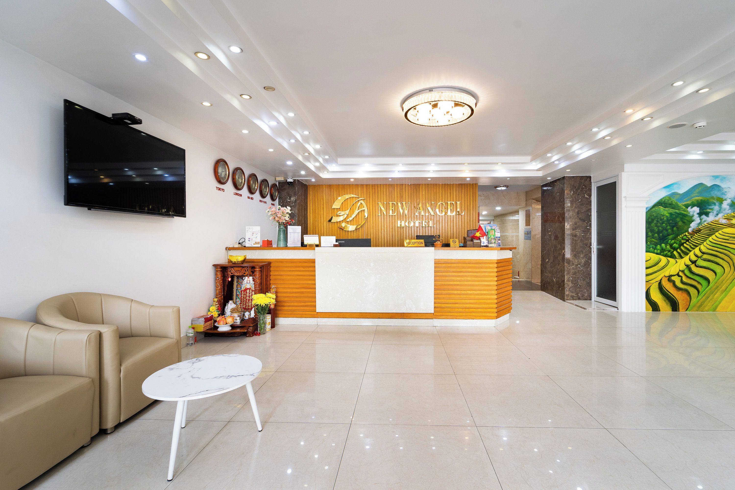 Uma área de recepção de hotel, com balcão de atendimento, televisão de tela plana, um sofá e uma mesa pequena.