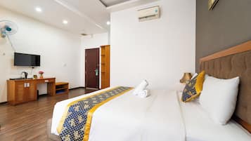 Quarto de hotel com cama, escrivaninha, televisão e ar condicionado.