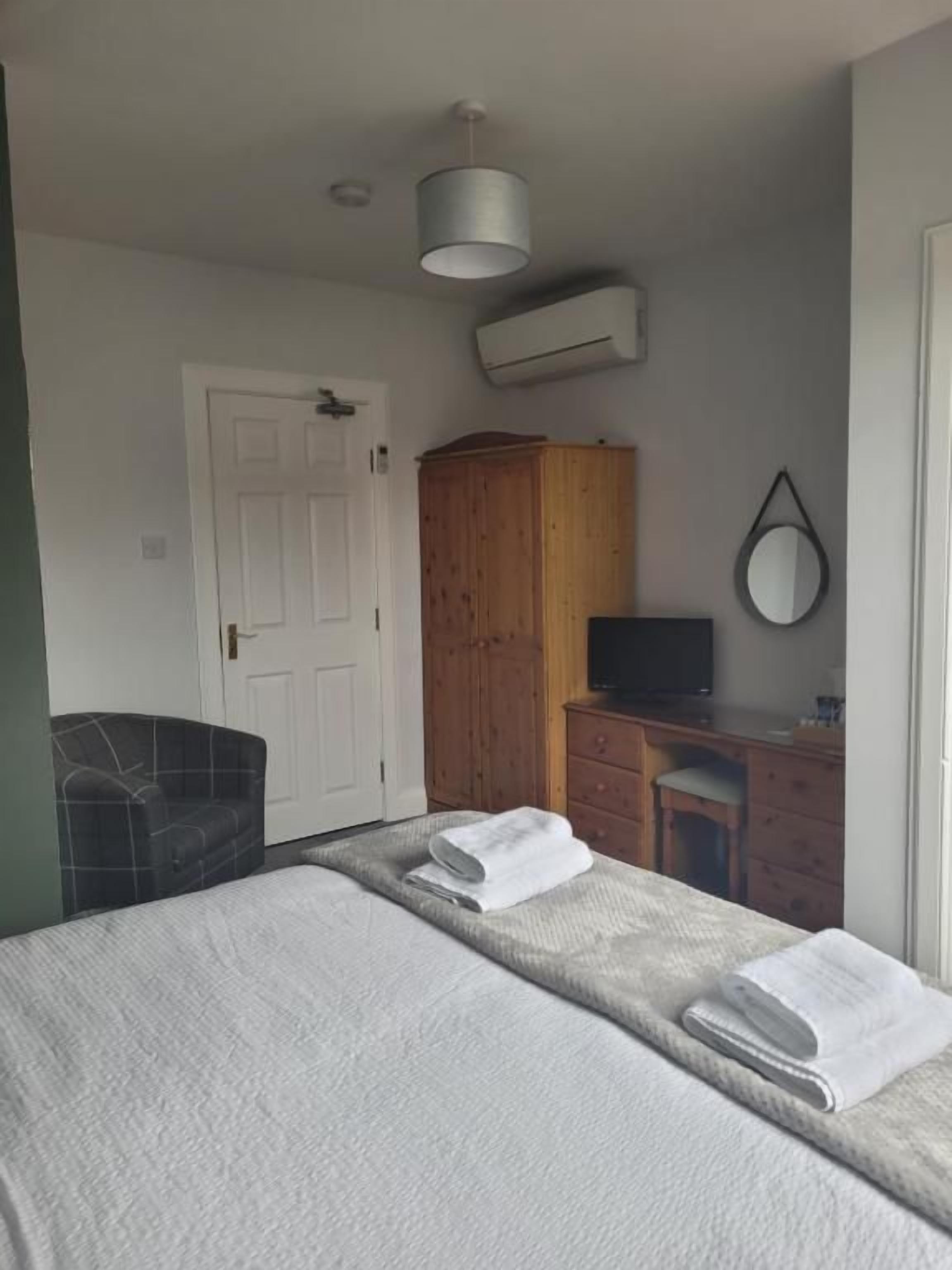 Quarto com cama, guarda-roupa de madeira, televisão e espelho na parede.