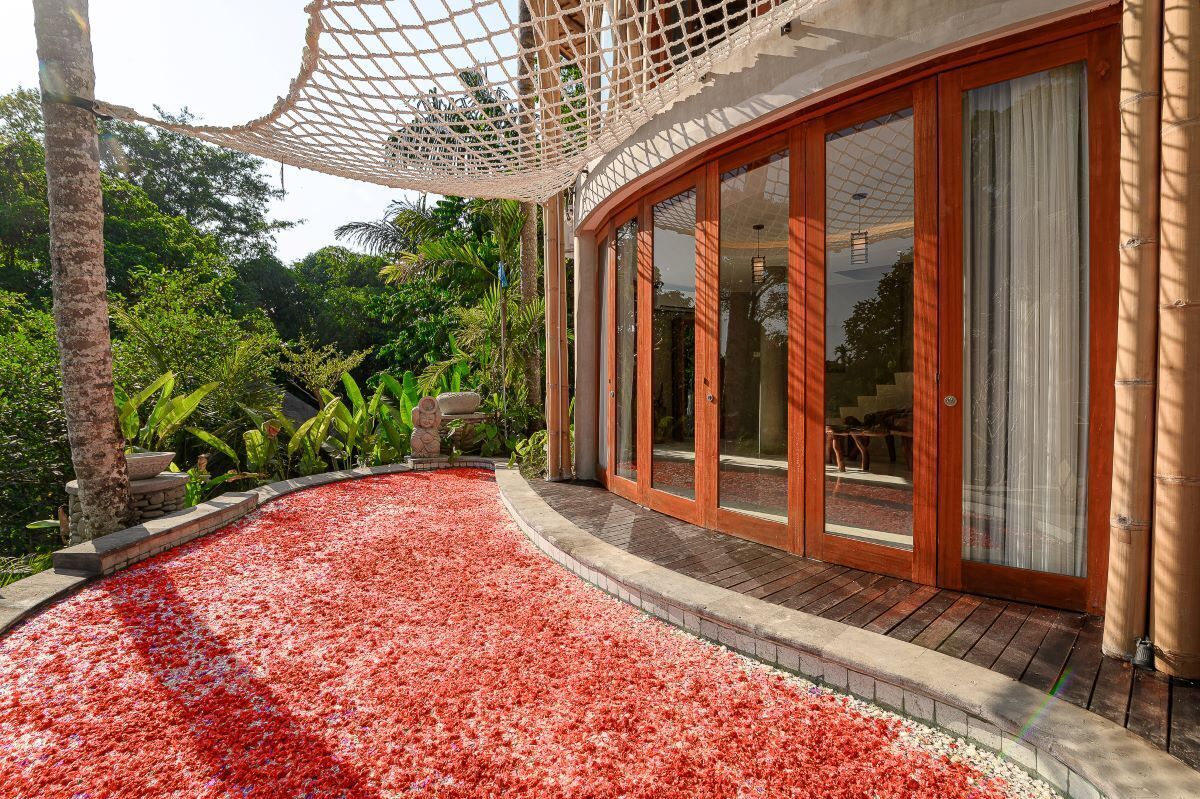 Uma villa moderna com um deck curvo de madeira, grandes portas de correr de vidro e uma pérgula com tela.