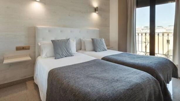Quarto de hotel moderno com duas camas, uma janela grande e uma varanda.