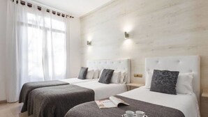 Quarto de hotel com duas camas, cada uma com cabeceira branca e roupa de cama cinzenta. Há uma janela com cortinas brancas e um tabuleiro com chá na cama.