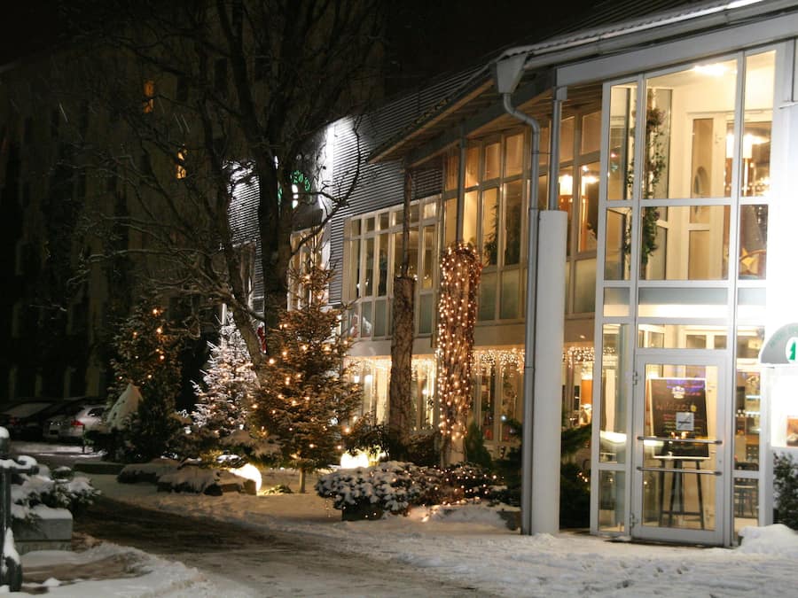 Um edifício com fachada de vidro, chão coberto de neve e luzes de Natal.