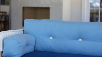 Um sofá azul com botões brancos, um travesseiro branco e uma cadeira branca num quarto com lareira e estante de livros.