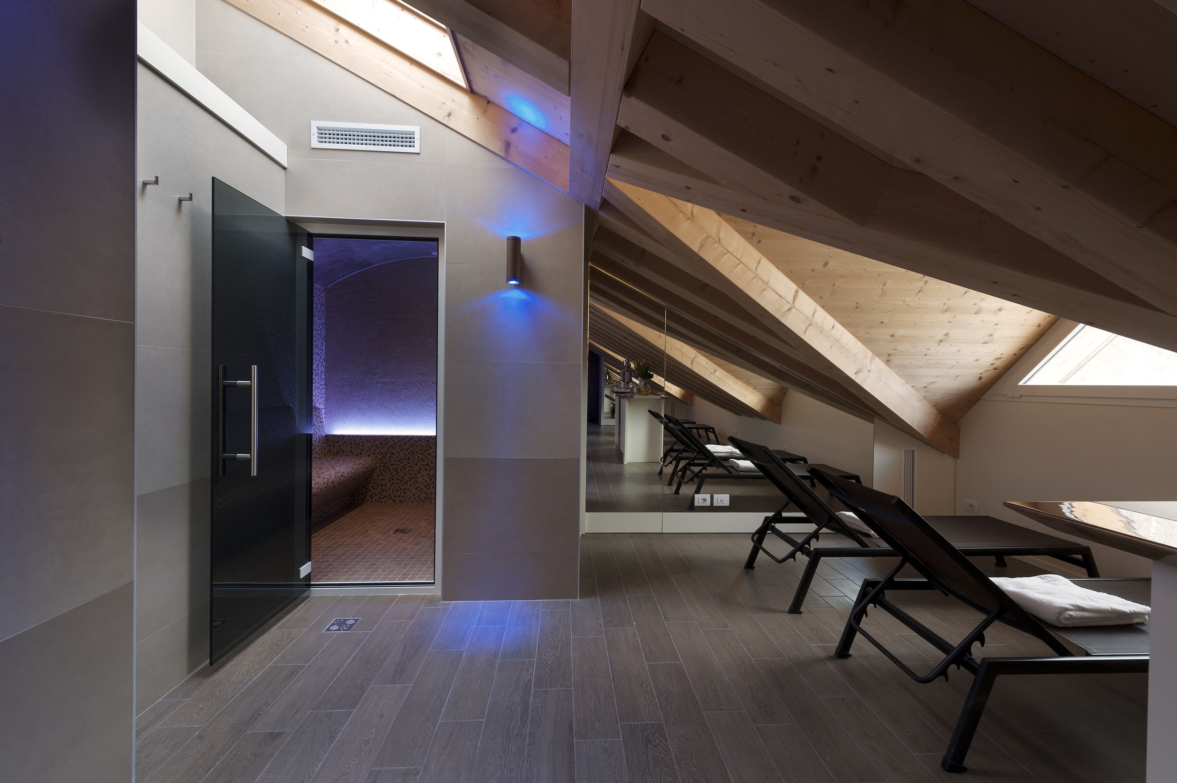Quarto de sótão moderno e espaçoso, com teto inclinado, porta de vidro para um recanto aconchegante e poltronas reclináveis com vista para o céu.