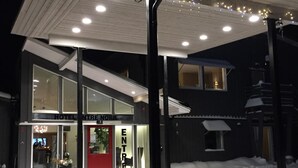 Entrada de hotel com porta vermelha, área externa coberta e neve no chão.