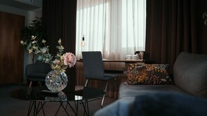 Uma sala de estar moderna com uma mesa de centro de vidro, um sofá com almofada estampada e uma poltrona.