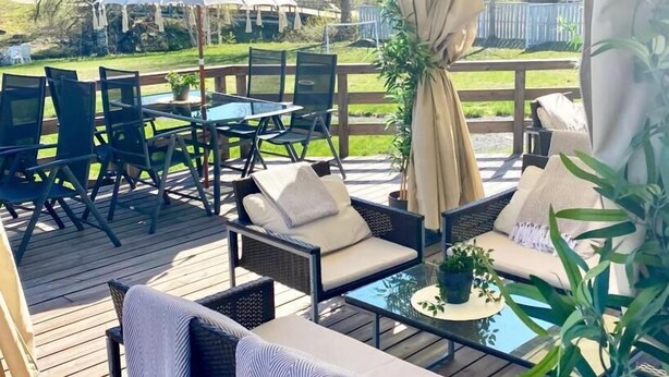 Um pátio coberto com móveis de vime, uma mesa de vidro e uma piscina ao fundo.