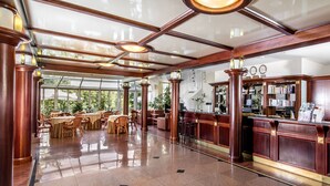 Um hall amplo com área de bar, espaços de estar e uma grande janela de vidro que permite a entrada de luz natural.
