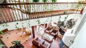 Ampla sala de estar com escada de madeira, sofás de couro, mesa de centro de vidro e diversos vasos de plantas.