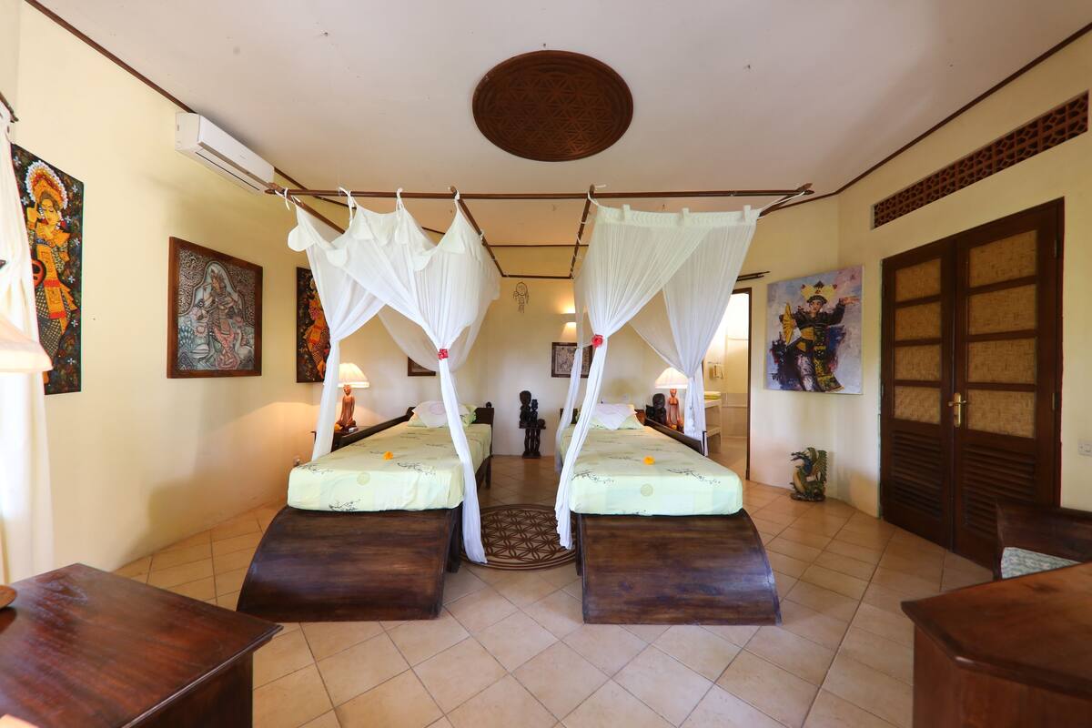 Quarto com duas camas, cada uma com dossel, um tapete redondo decorativo e uma porta de madeira grande.