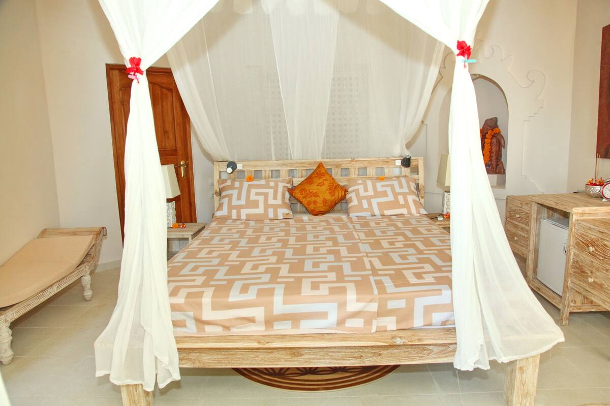 Uma cama com dossel, cabeceira de madeira, roupa de cama estampada e uma almofada decorativa.