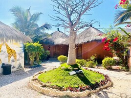 Uma área de recepção com uma placa, uma árvore e cabanas com telhado de palha.