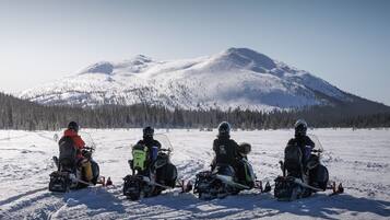 Três motos de neve em um campo coberto de neve, com uma montanha ao fundo.